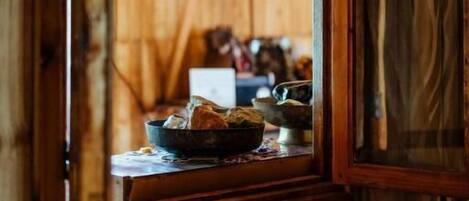 Interior de madeira com uma janela mostrando um quarto com uma mesa, uma tigela e uma cadeira.