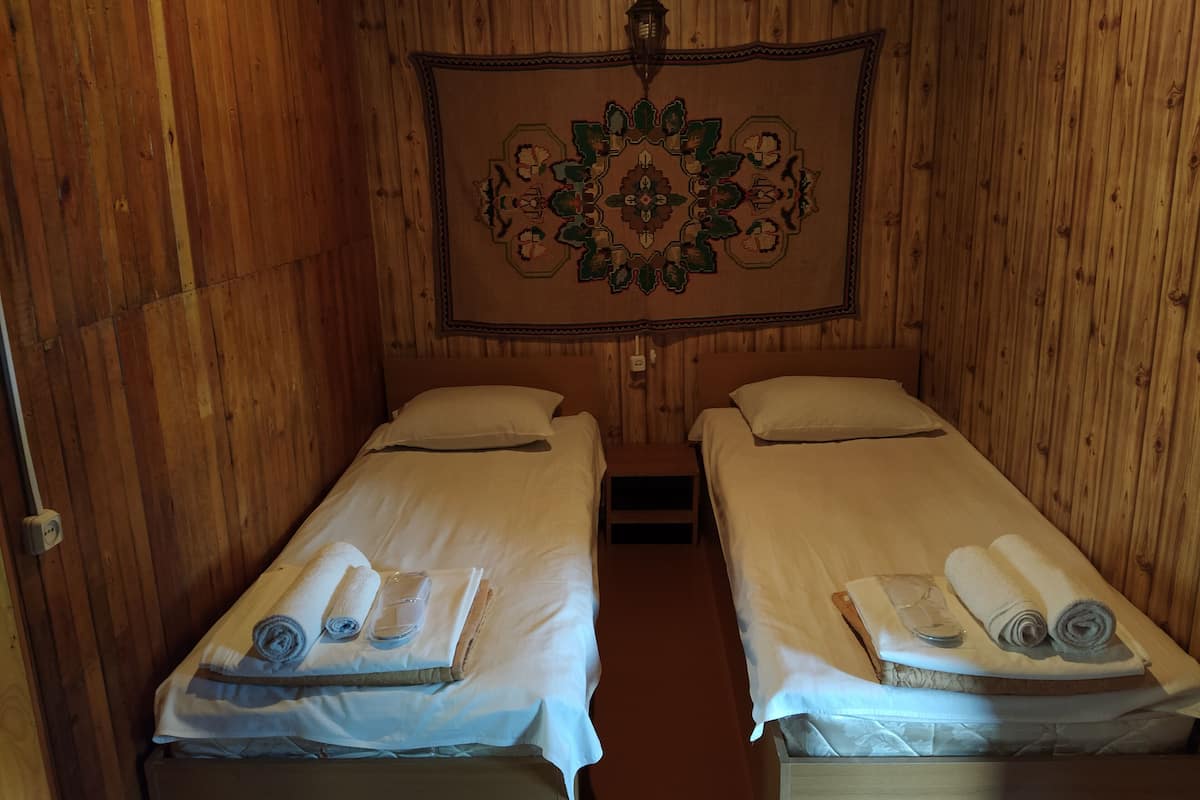Quarto de madeira com duas camas, cada uma com uma toalha enrolada e um copo de água.