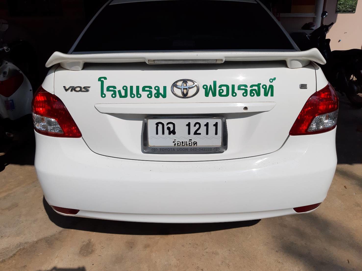 Parte traseira de um Toyota Vios branco com a placa de identificação numérica '1211'.