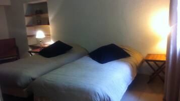 Quarto duplo com duas camas de solteiro, uma mesinha de cabeceira com luminária e uma pequena mesa.