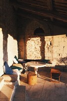 Um quarto com paredes de pedra, uma mesa redonda e um pequeno banquinho de madeira.