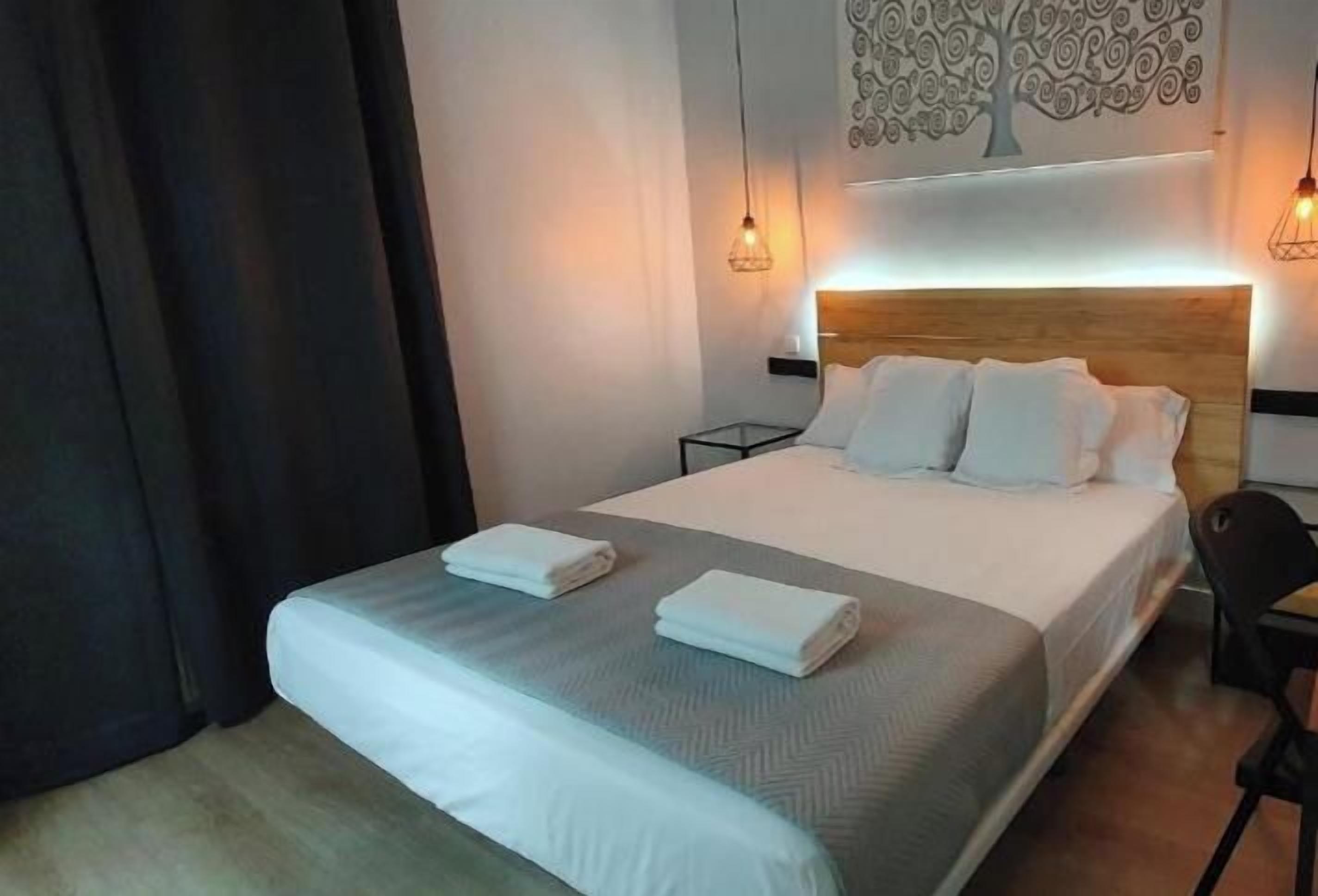 Quarto de hotel com uma cama grande, cabeceira, duas mesinhas de cabeceira, uma cadeira e uma obra de arte pendurada na parede.