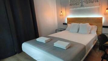 Quarto de hotel com uma cama grande, cabeceira, duas mesinhas de cabeceira, uma cadeira e uma obra de arte pendurada na parede.