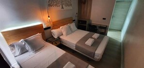 Quarto de hotel com duas camas, uma mesa de cabeceira, uma luminária e uma obra de arte na parede.
