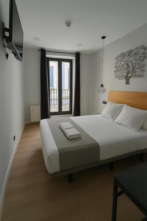 Quarto de hotel moderno com uma cama grande, televisão de tela plana, varanda com cortinas e um detalhe decorativo na parede.