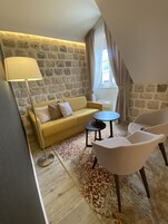 Uma sala de estar aconchegante com parede de pedra, um sofá amarelo, um abajur, uma mesinha redonda e duas cadeiras.