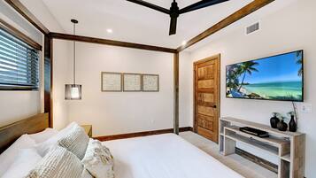 Quarto com cama, ventilador de teto, TV sobre um console de madeira e porta com painel de madeira.