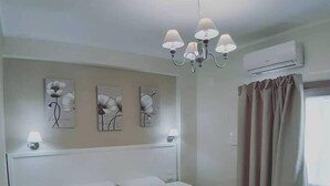 Quarto com cama grande, mesas de cabeceira, lustre, obras de arte na parede e ar condicionado.