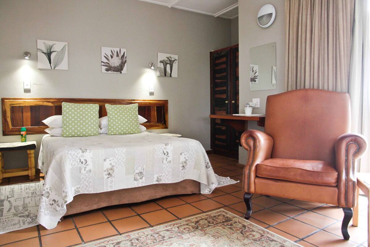Quarto com cama, cadeira, escrivaninha e obras de arte nas paredes.