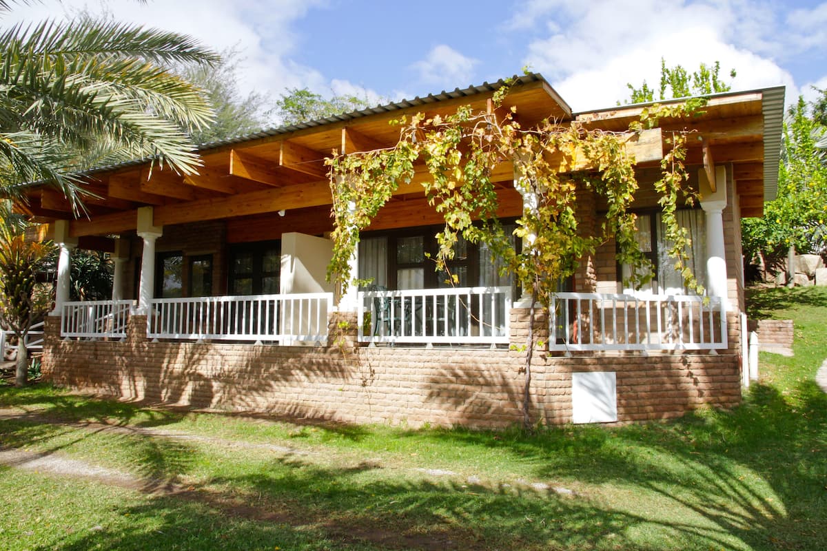 Uma casa de dois andares com varanda coberta, paredes de tijolo e um pequeno jardim.