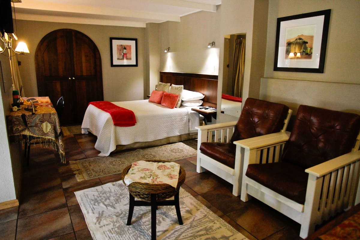 Quarto de hotel com cama, cadeira, mesa pequena e escrivaninha.