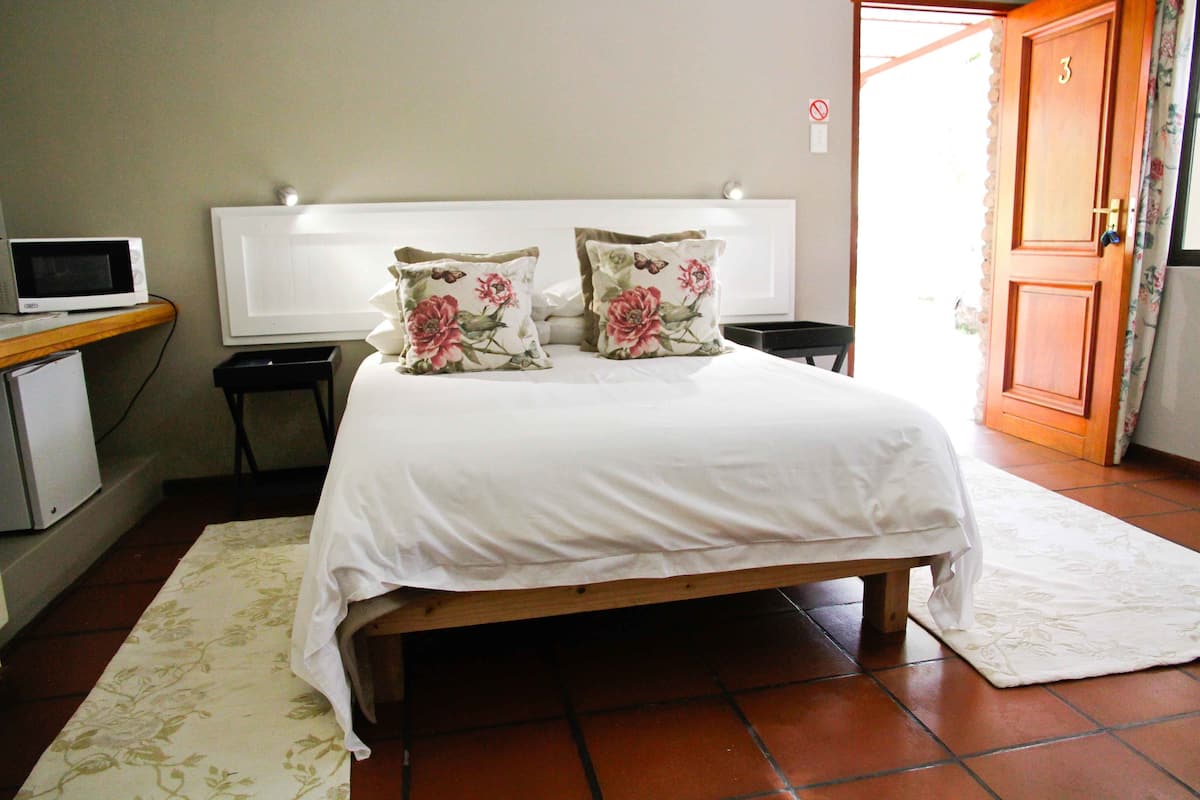 Quarto com cama, duas mesinhas de cabeceira, um criado-mudo, micro-ondas e uma porta.