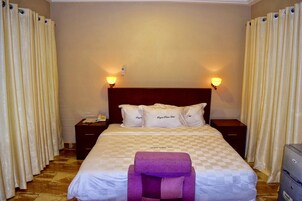 Quarto de hotel com colcha xadrez, duas mesas de cabeceira com abajures e toalha roxa na cama.