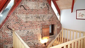 Interior com paredes de tijolo, uma escada de madeira e um pequeno armário de madeira.