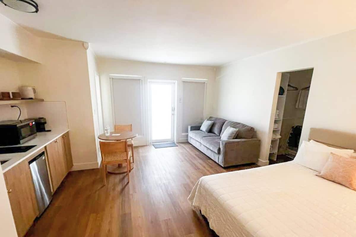 Quarto de hotel compacto com cama, sofá, mesinha e cozinha compacta.