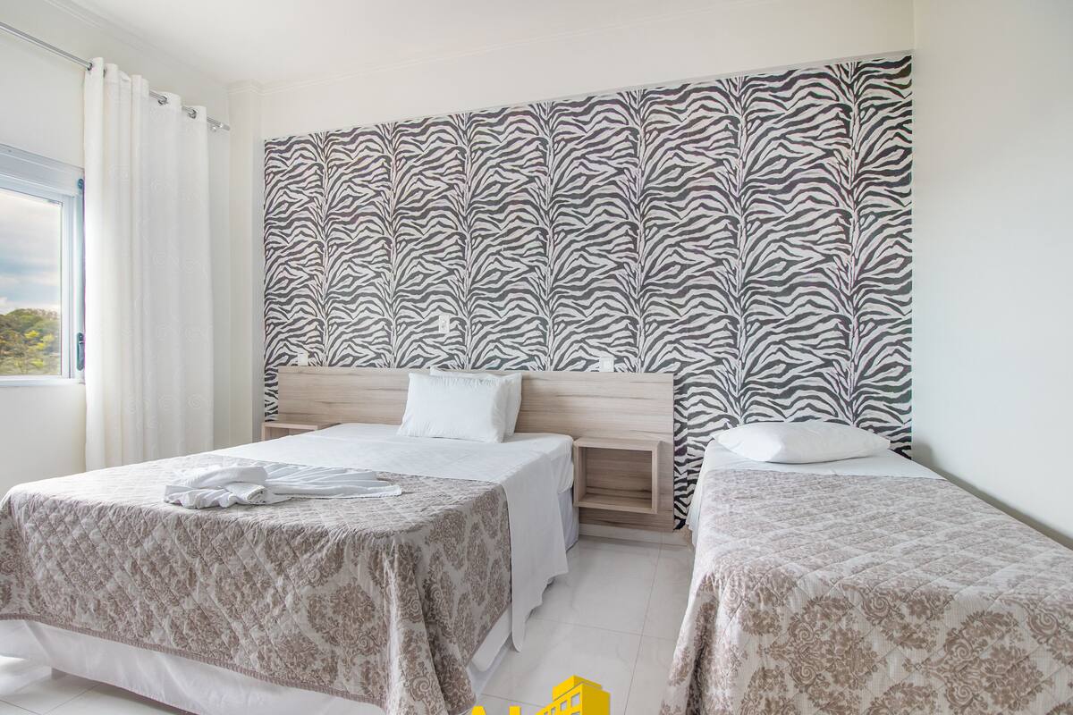 Quarto de hotel com duas camas, parede com padrão de zebra e janela com cortinas.