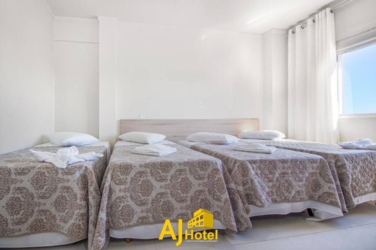 Quarto de hotel com quatro camas individuais, cada uma com colcha estampada e almofadas brancas.