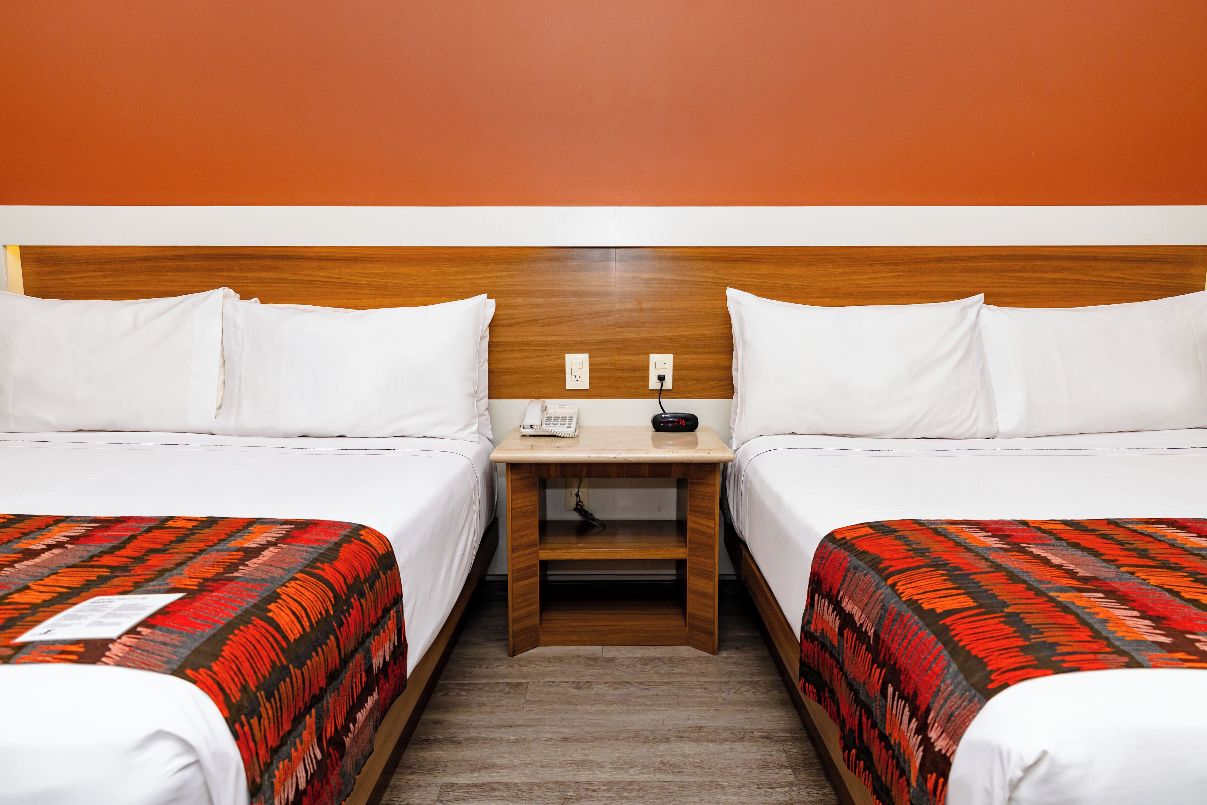 Quarto de hotel com duas camas, uma mesinha de cabeceira de madeira e um telefone.