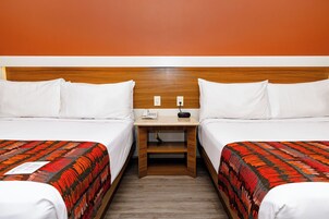 Quarto de hotel com duas camas, uma mesinha de cabeceira de madeira e um telefone.