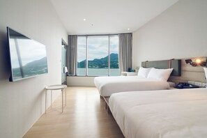 Quarto de hotel moderno com duas camas, uma janela grande com vista para as montanhas, uma televisão de tela plana e uma pequena mesinha.