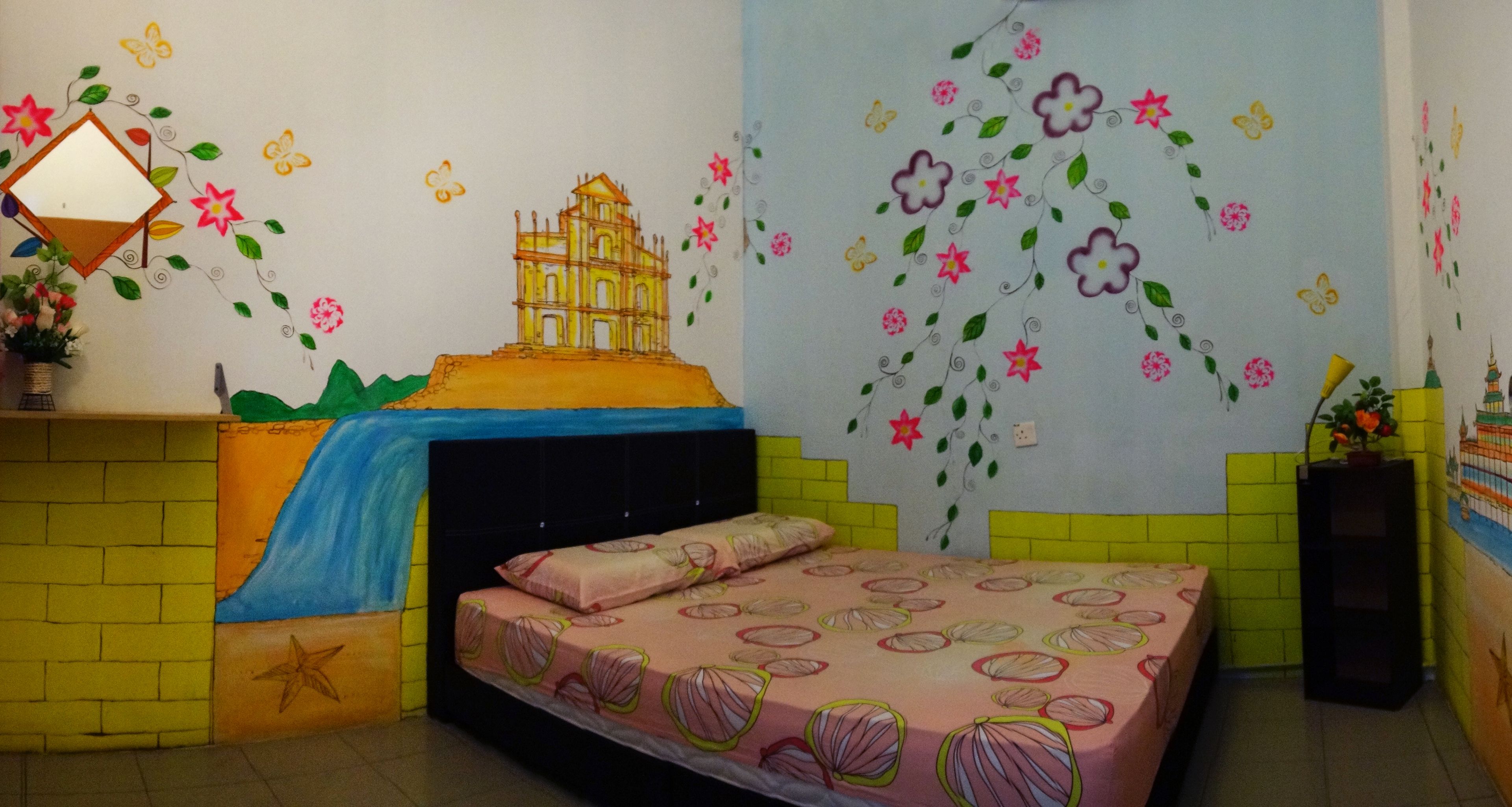 Um quarto com uma cama, um mural na parede e uma pequena mesa com um vaso de flores.