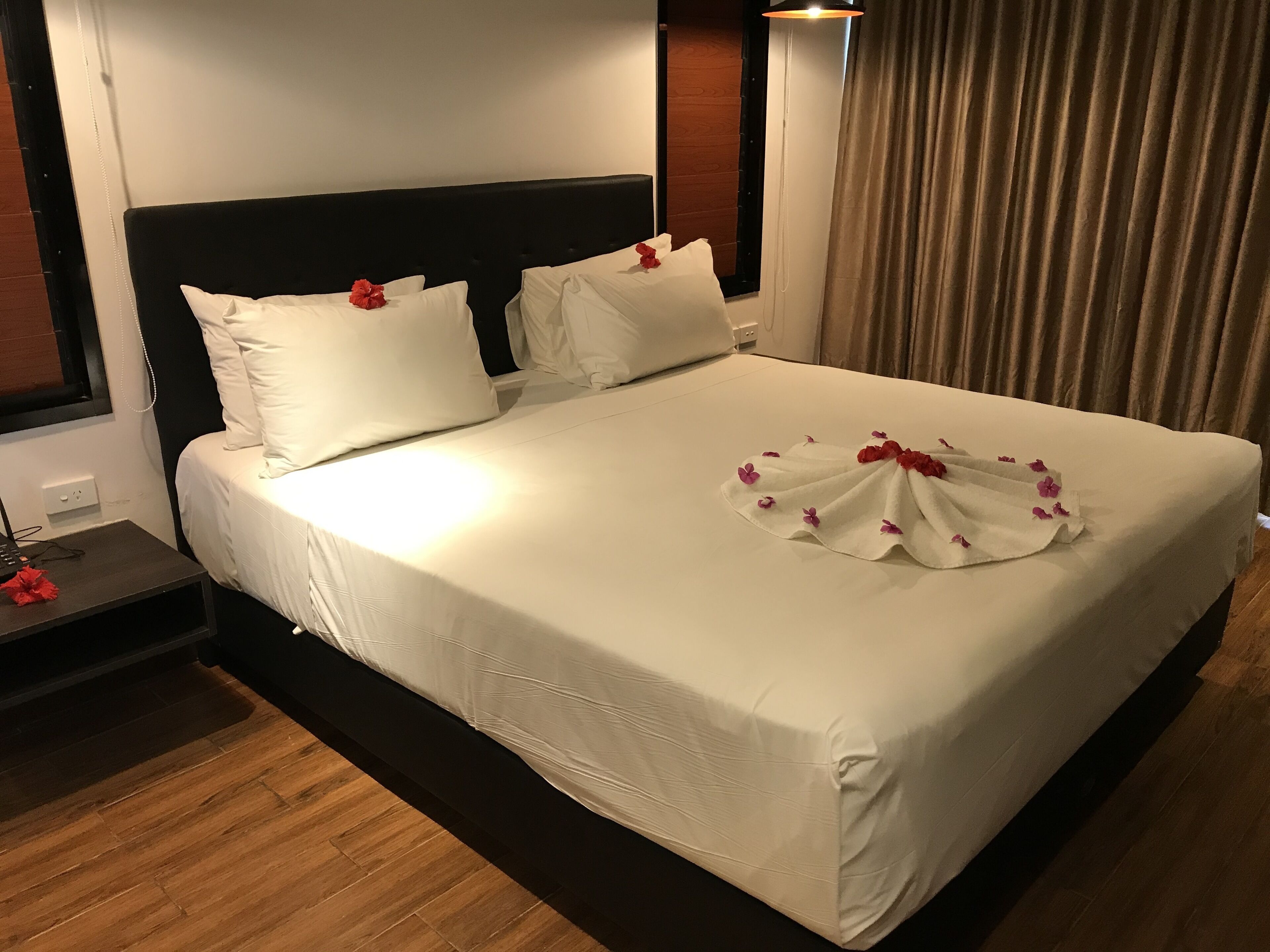 Cama bem arrumada com roupa de cama branca e um arranjo floral sobre o edredom.