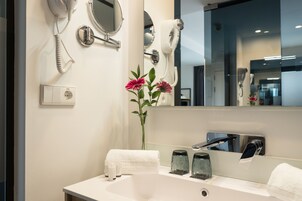 Uma casa de banho moderna com lavatório branco, espelho, secador de cabelo e um vaso com flores.