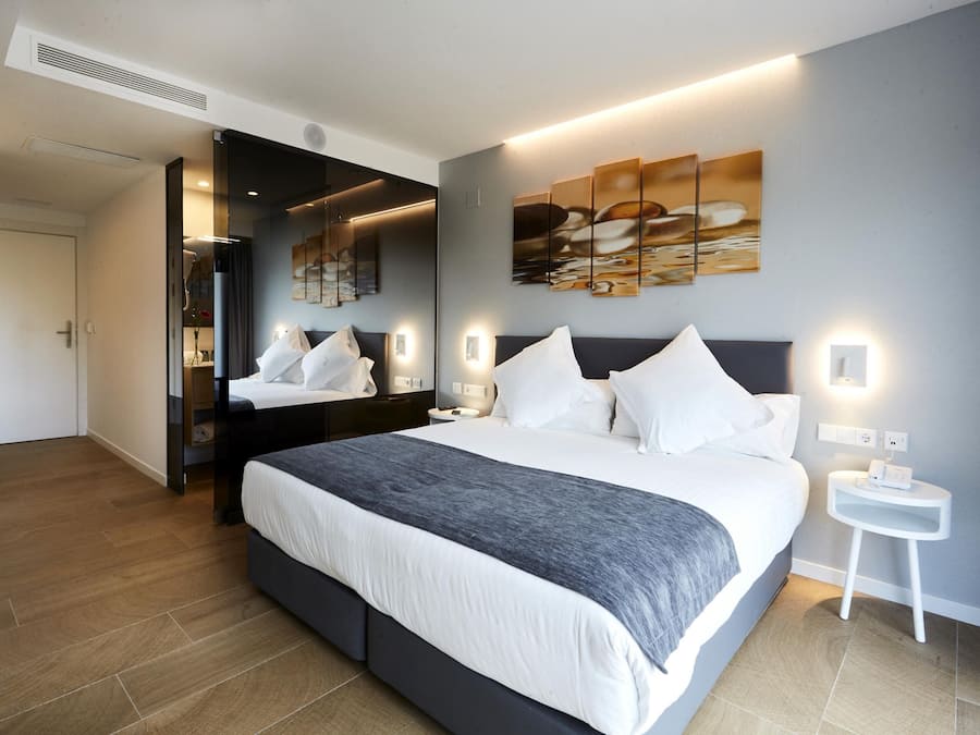Quarto de hotel moderno com uma cama grande, mesas de cabeceira, um espelho e obras de arte na parede.