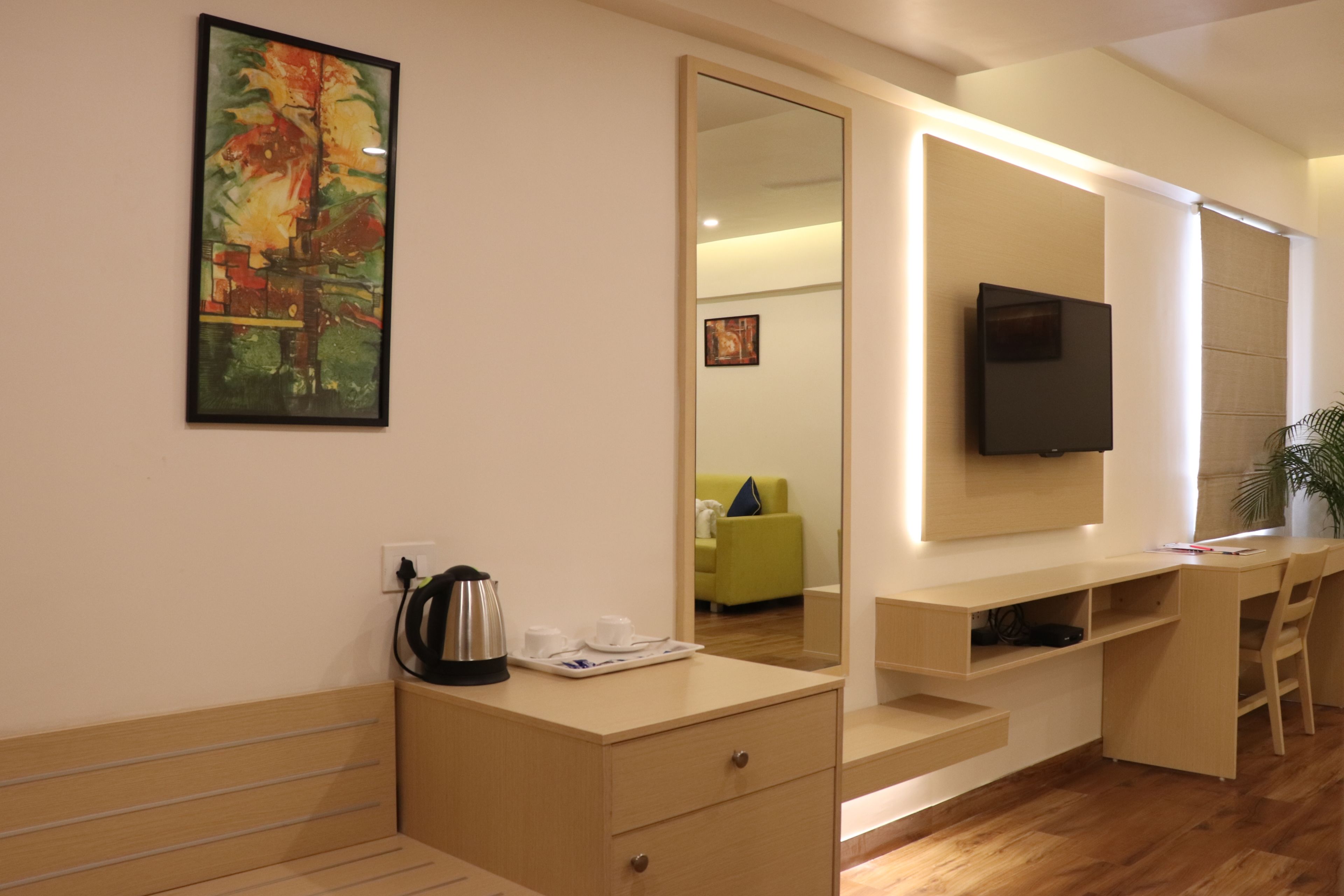 Quarto de hotel moderno com escrivaninha de madeira, TV de tela plana, pintura na parede e cafeteira no criado-mudo.