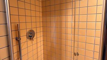 Um pequeno banheiro com azulejos, chuveiro manual e painel de controle na parede.