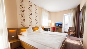 Quarto de hotel com uma cama grande, uma escrivaninha com computador, uma cadeira e uma televisão.
