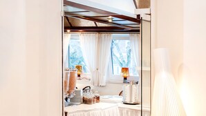 Quarto de hotel com um espelho grande refletindo um banheiro, uma poltrona de couro vermelha e um abajur.