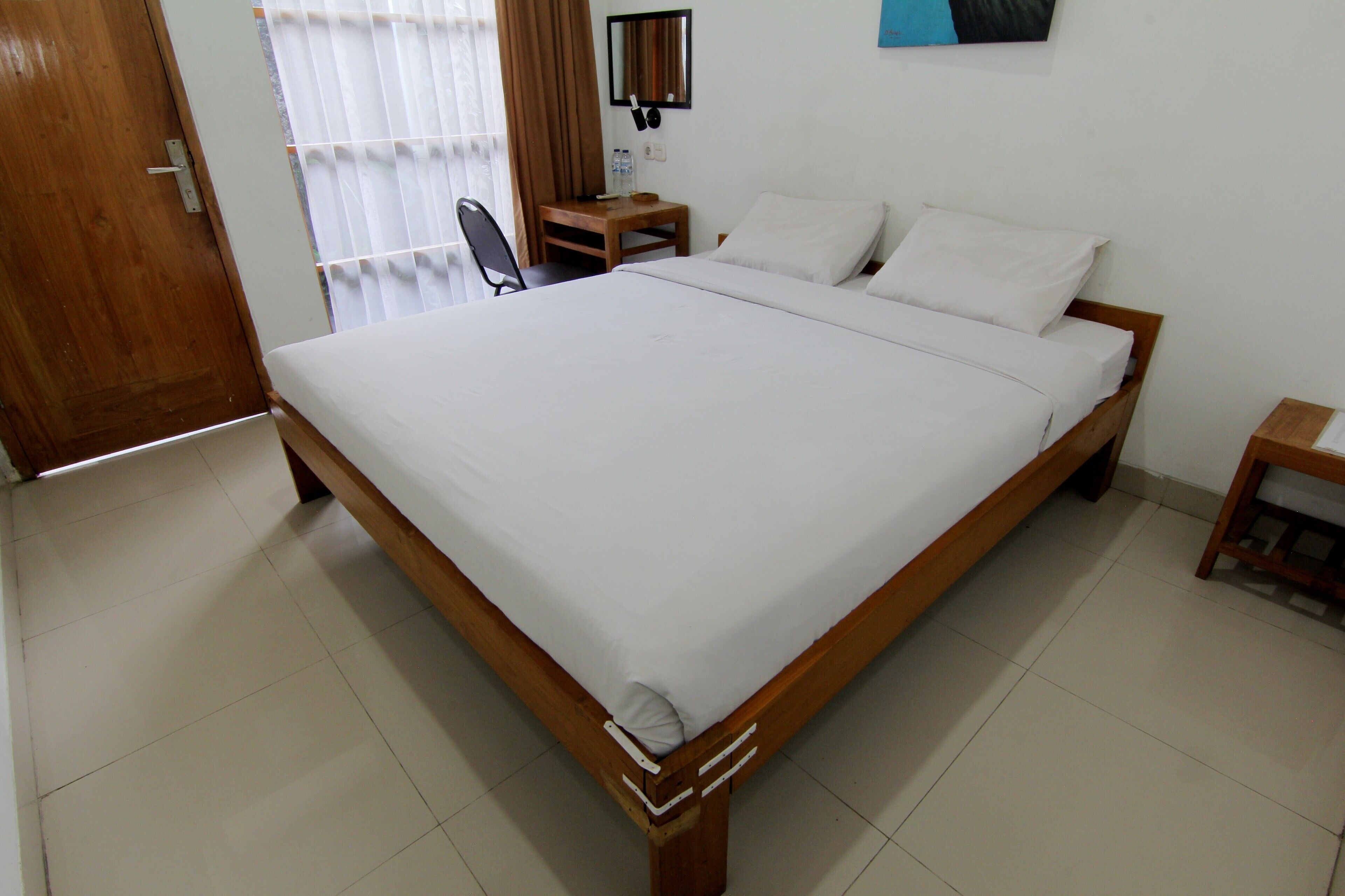 Quarto de hotel com uma cama grande, uma escrivaninha de madeira, uma cadeira e uma mesinha.