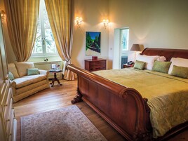Quarto com uma cama de madeira grande, cômoda de madeira, mesa pequena com abajur e um sofá.