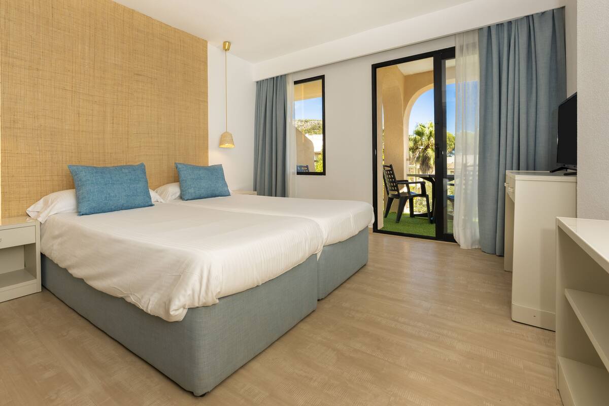 Quarto de hotel com uma cama grande, uma escrivaninha, uma cadeira e uma varanda com vista.