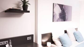 Quarto moderno com cama, mesa de cabeceira e prateleira na parede com uma planta.