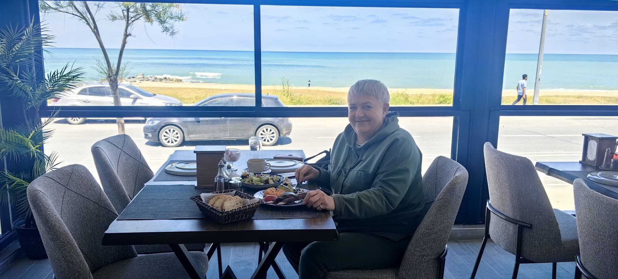 Uma pessoa jantando à mesa com vista para a praia e o oceano.