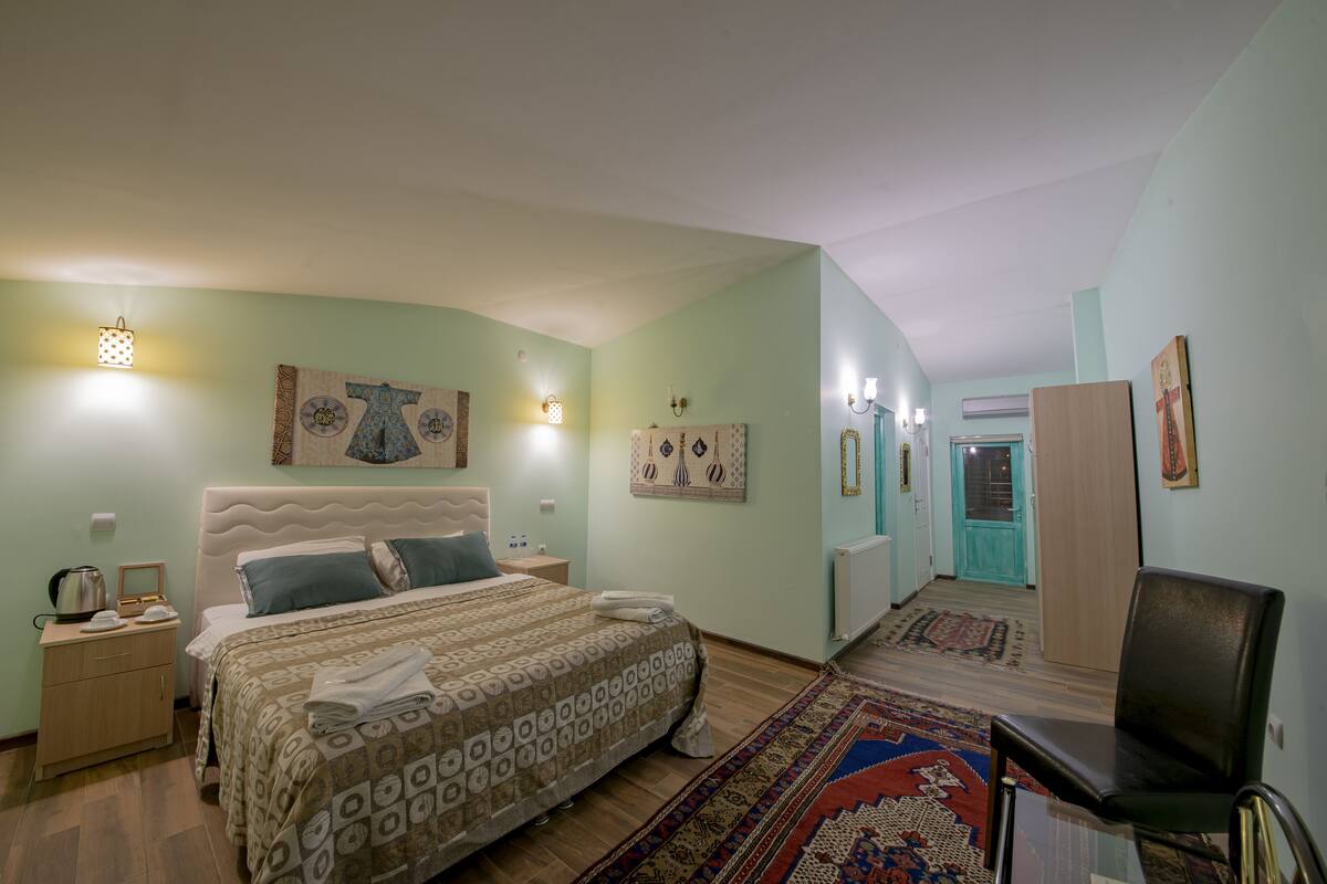 Quarto com cama, mesas de cabeceira, uma cadeira e porta que dá para outro cômodo.