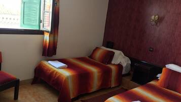 Quarto de hotel com duas camas, janela com persianas verdes, parede vermelha e mesa de cabeceira com abajur.