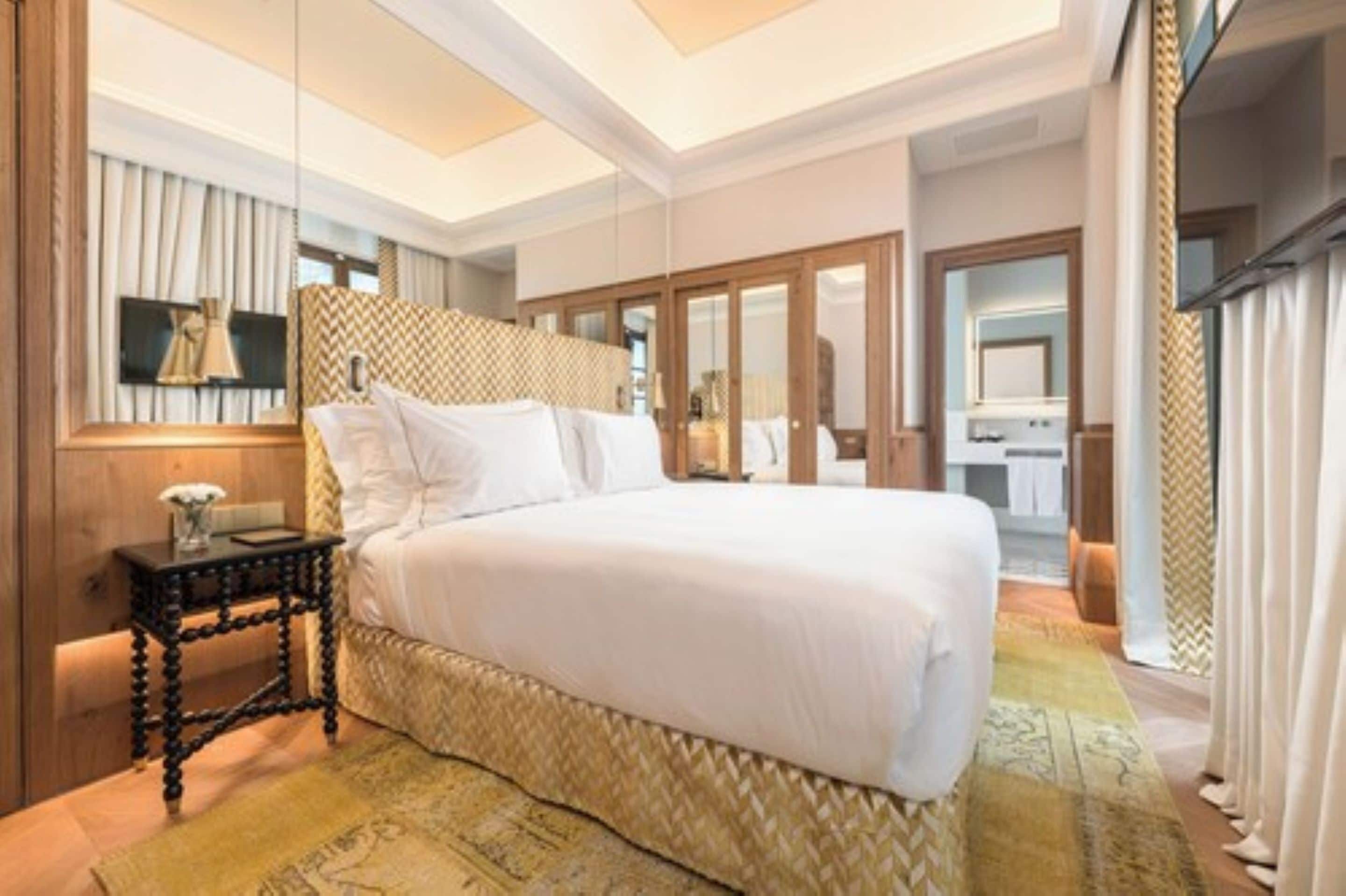 Quarto de hotel com uma cama grande, uma mesa de cabeceira, um espelho e vista para o banheiro.