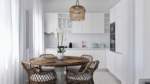 Cozinha moderna com armários brancos, uma mesa redonda de madeira com jogos americanos trançados, cadeiras de vime e um lustre de vime pendente.
