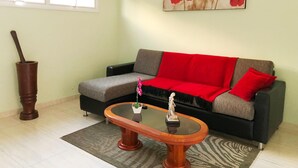Uma sala de estar com um sofá cinza, um cobertor vermelho, uma mesa de centro de madeira e um quadro de flores vermelhas na parede.
