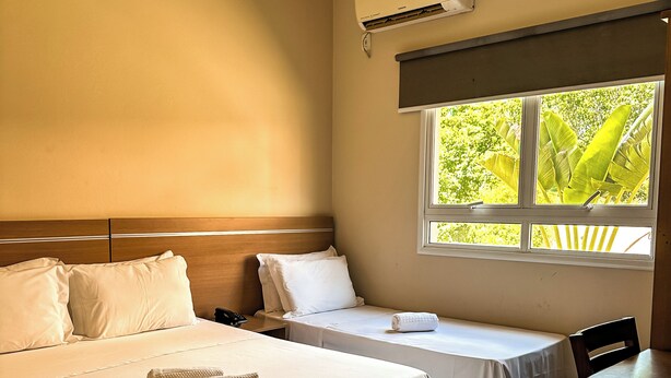Quarto de hotel com duas camas, uma escrivaninha e janela com vista para áreas verdes.