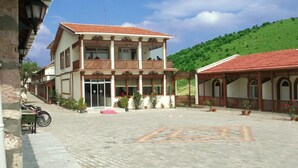 Um edifício de dois andares com telhado de telhas vermelhas, entrada coberta com um tapete vermelho e pátio pavimentado.