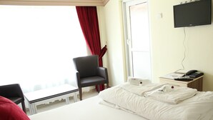 Quarto de hotel com cama, escrivaninha, cadeira, televisão e janela com cortinas.