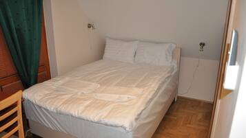 Uma cama pequena e bem arrumada num quarto com piso de madeira e cortina verde.