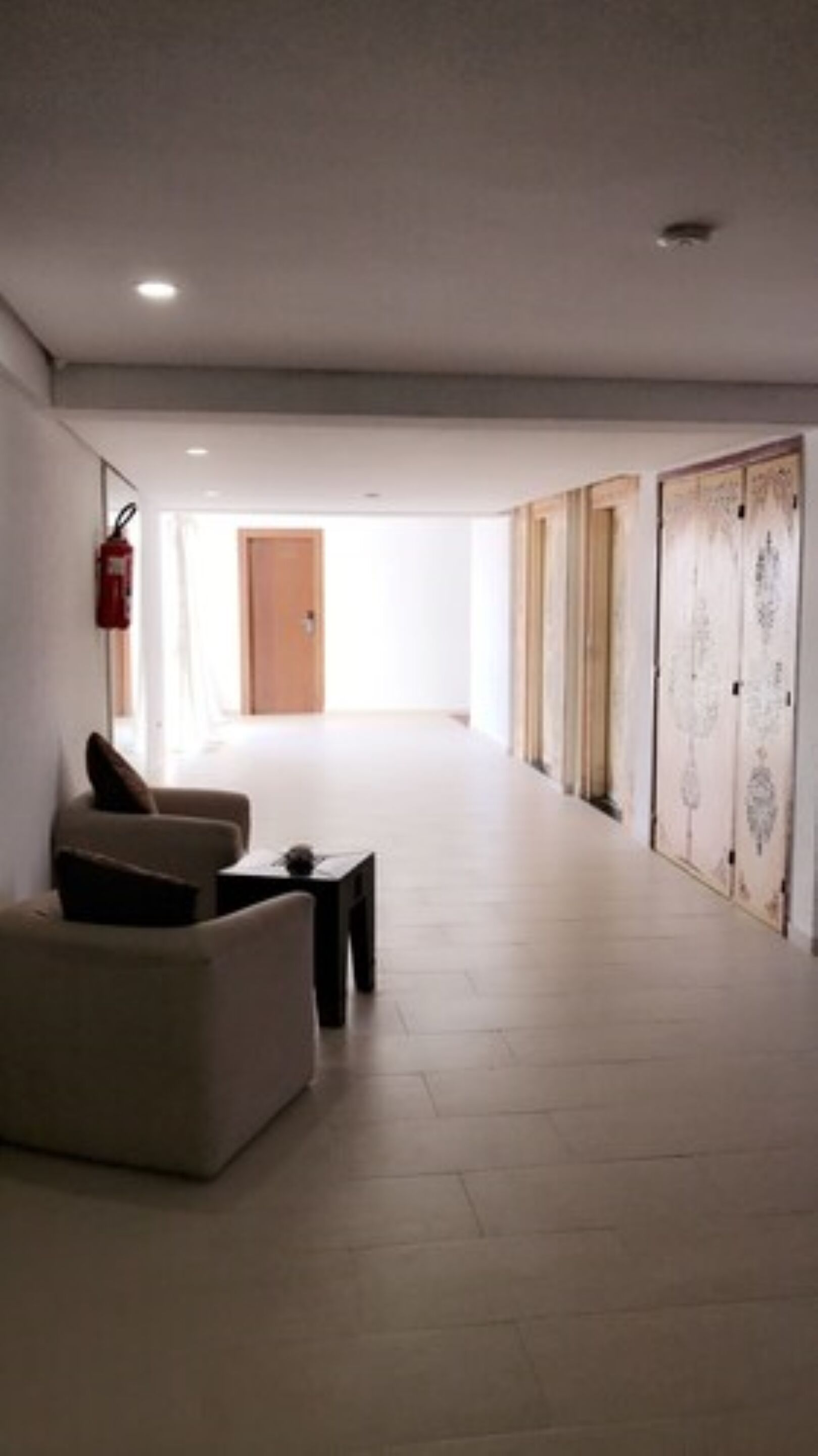 Corredor de hotel com sofá, uma pequena mesa e um extintor de incêndio na parede.