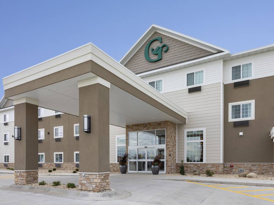 Hotel com design moderno, exibindo um logotipo 'G' em destaque na fachada, entrada coberta e parede de tijolos.
