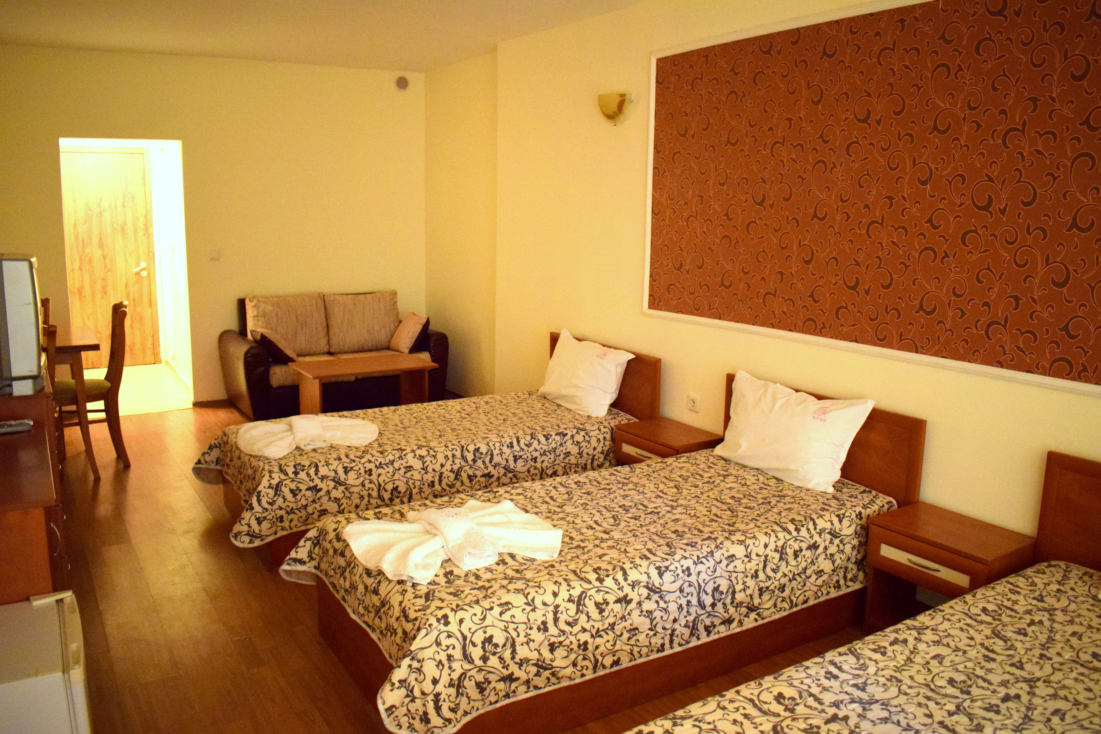 Quarto de hotel com três camas, uma escrivaninha, uma cadeira e um grande papel de parede estampado.