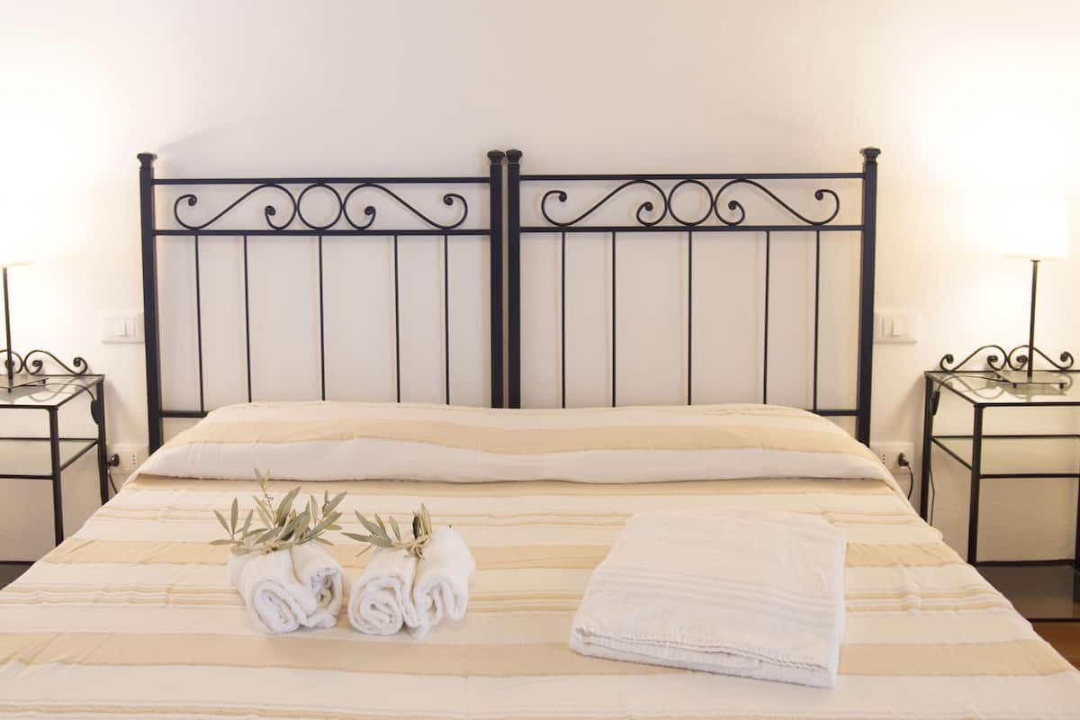 Cama bem arrumada com colcha listrada, duas mesas de cabeceira com luminárias e um cabeceiro decorativo.